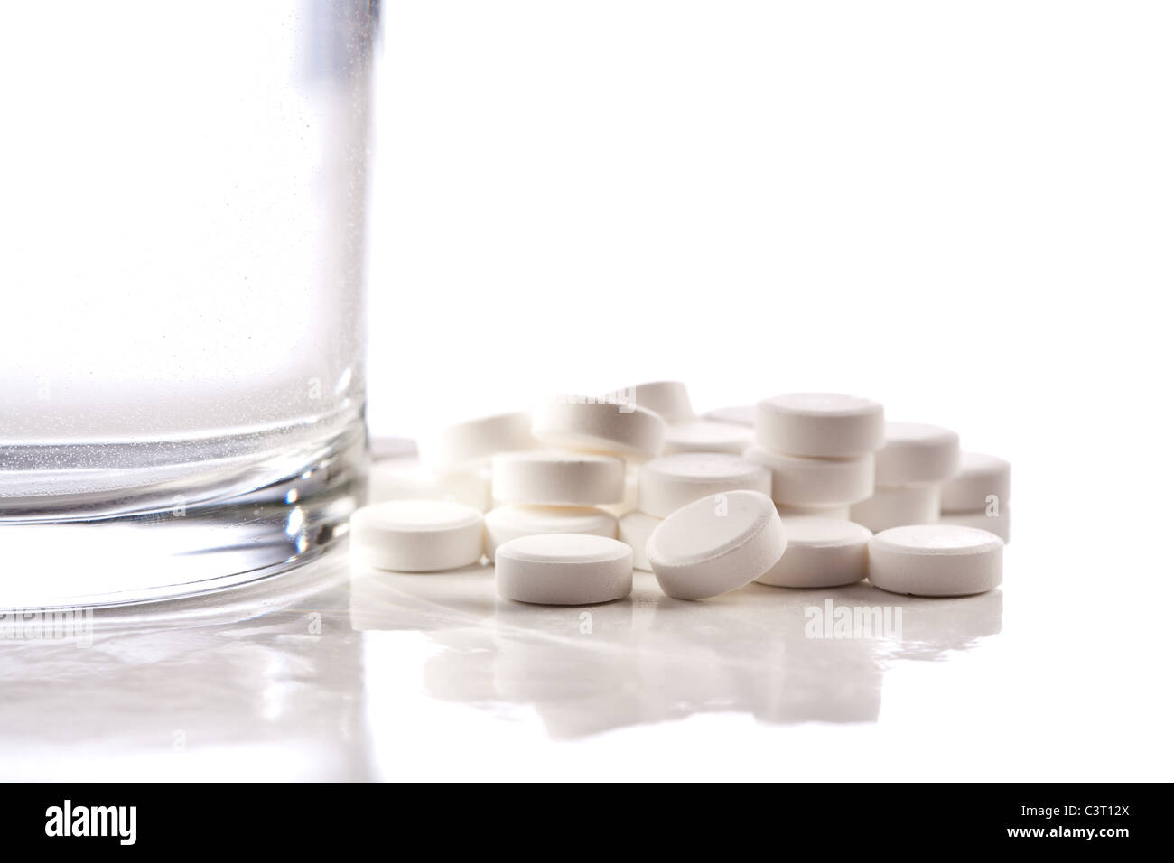 A pile of white tablets near a glass of water isolated on white ...