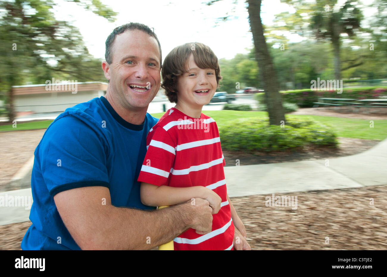 Father and son having fun laughing on merry go round spinning in ...