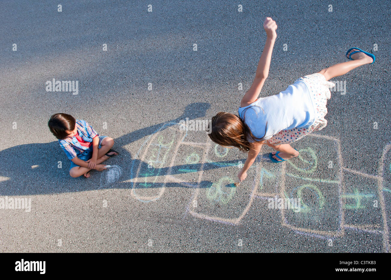 Graphic angle of young girl playing hopskotch on pavement from above ...