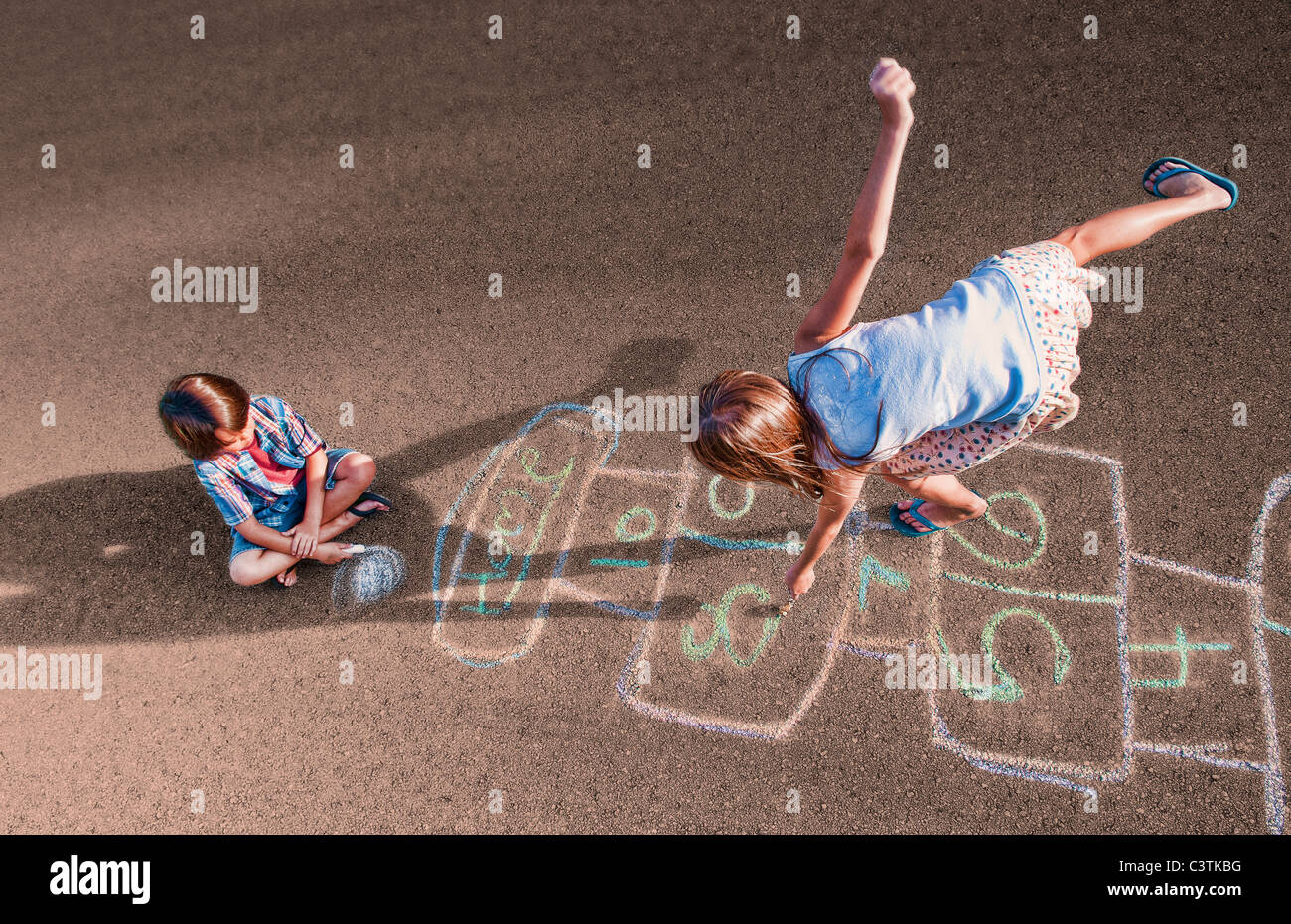 Graphic angle of young girl playing hopskotch on pavement from above ...