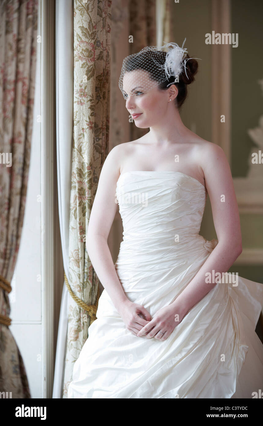 Pretty bride looking out of window and smiling on her wedding day Stock ...