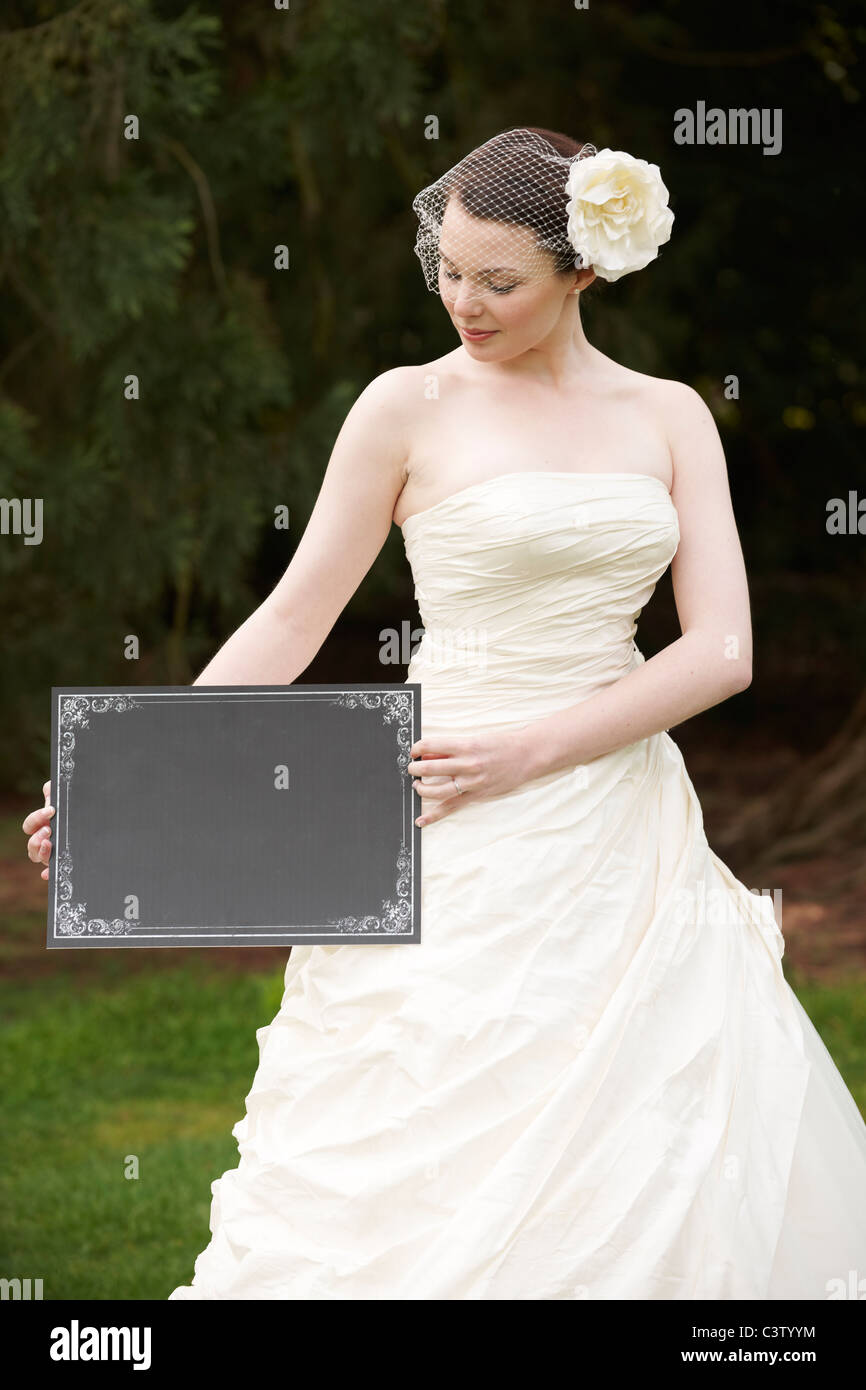 Pretty bride in wedding dress holding a blank board with space for copy ...