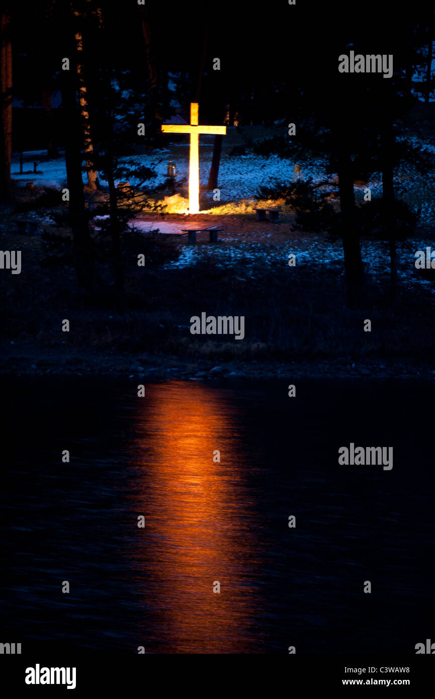 A spotlit cross is reflected at night in the calm water of Salmon Lake ...