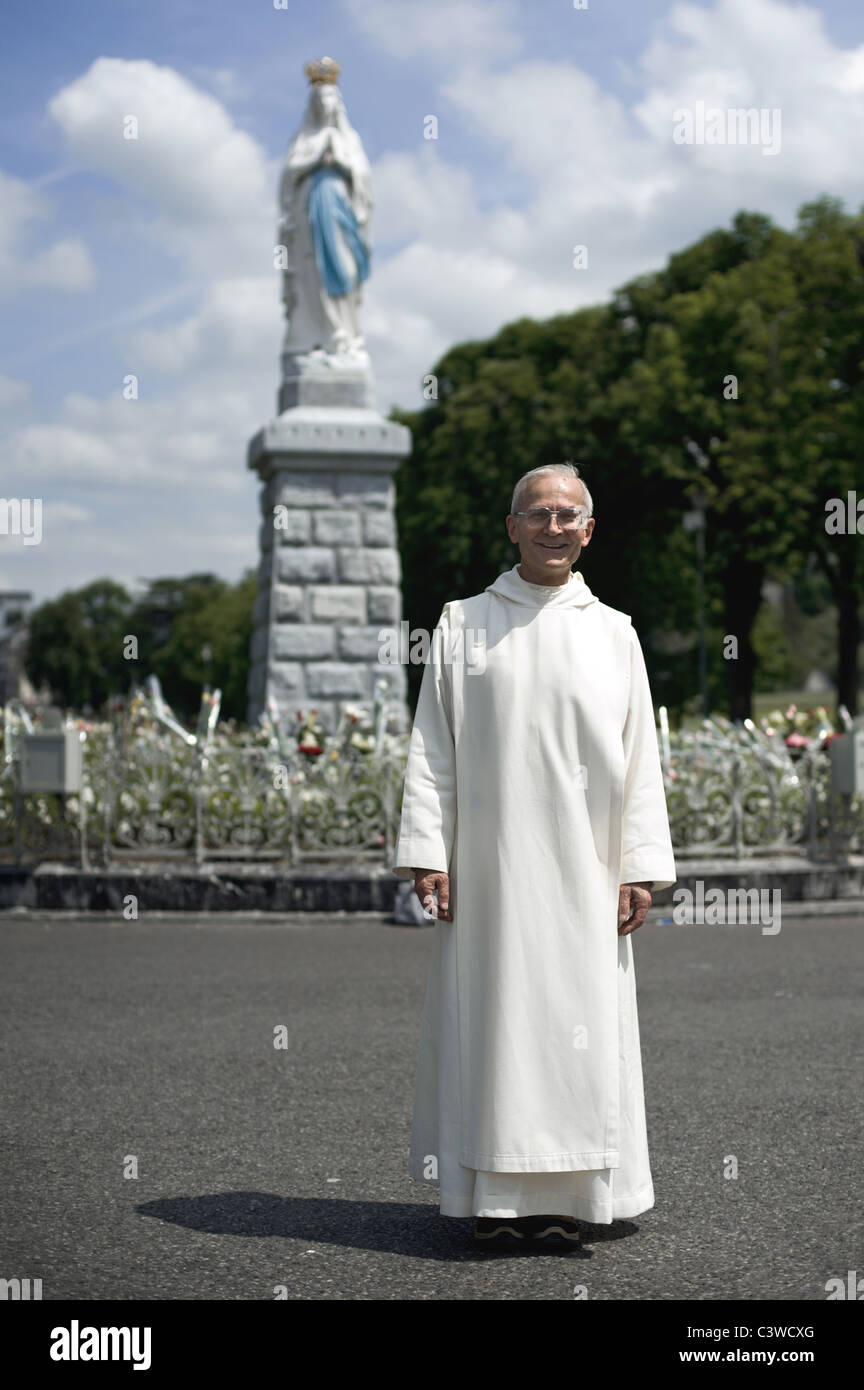 A Catholic Priest stands infront of the statue of Our Lady of Lourdes ...
