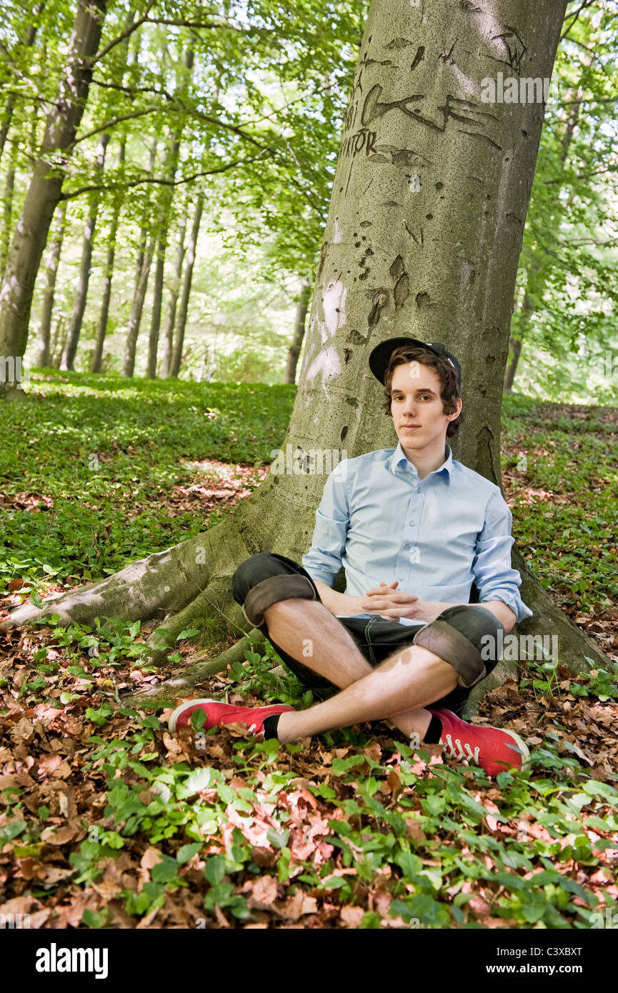 Young man sitting in front of a tree in the woods Stock Photo - Alamy