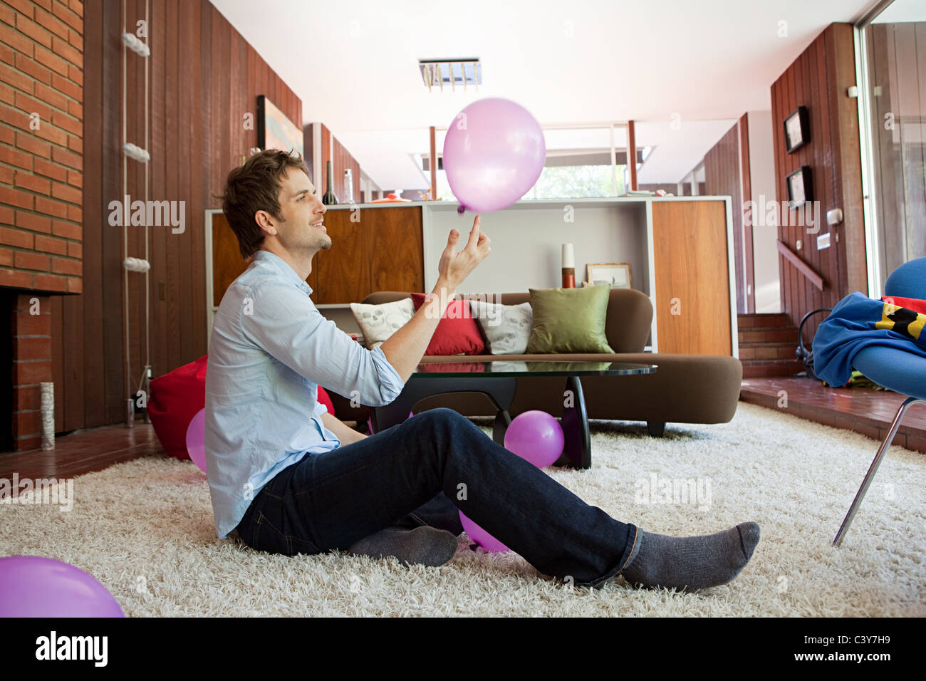 Man sitting on living room floor playing with pink balloon Stock Photo ...
