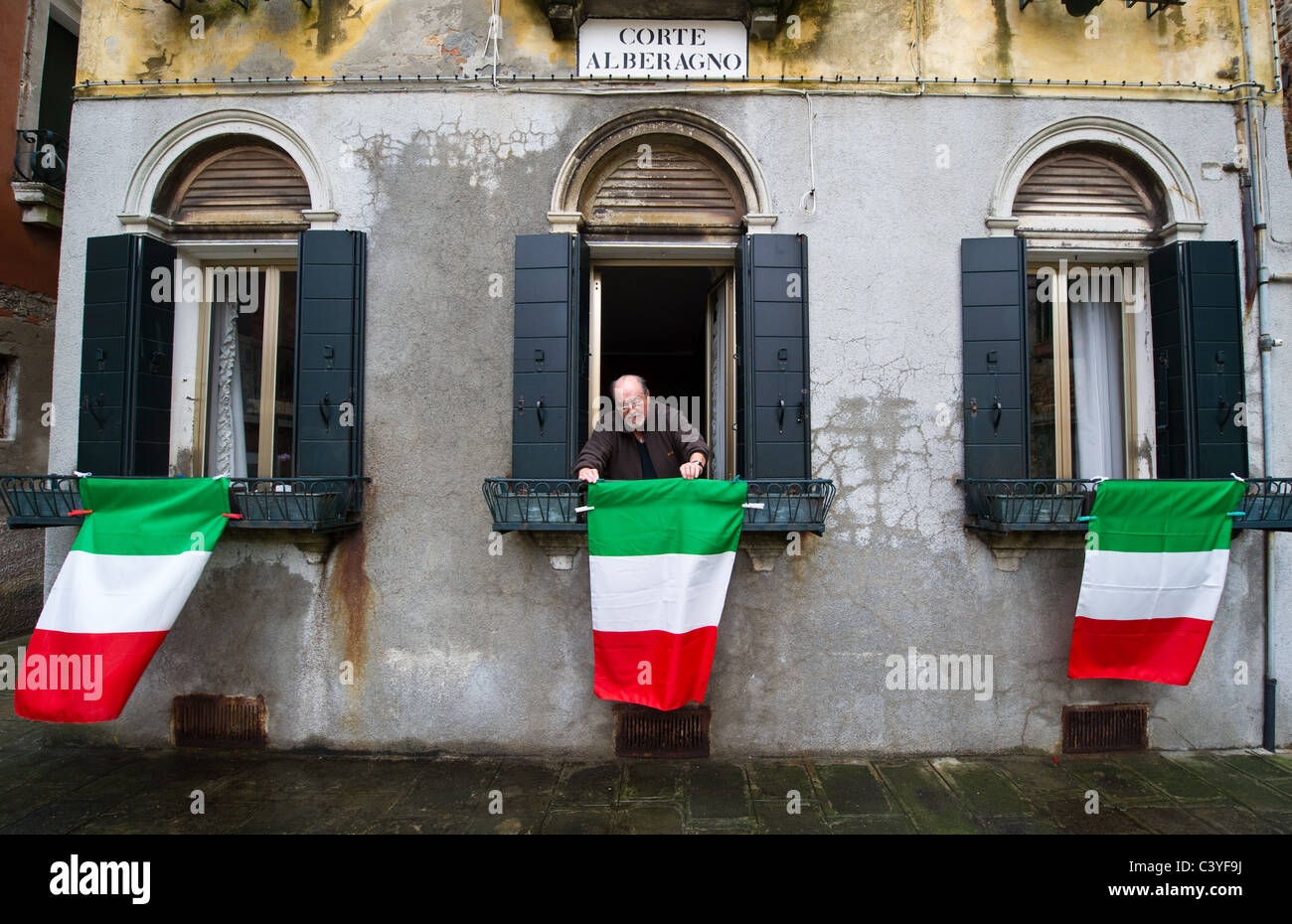 A man arranging three italian flags hanging from the windows of a house ...