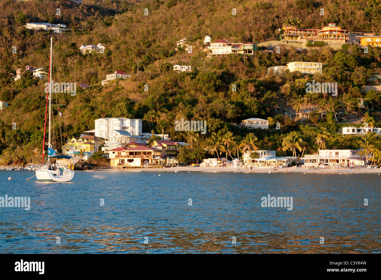 Evening glow on the pretty hillside homes above the beach with sailboat ...
