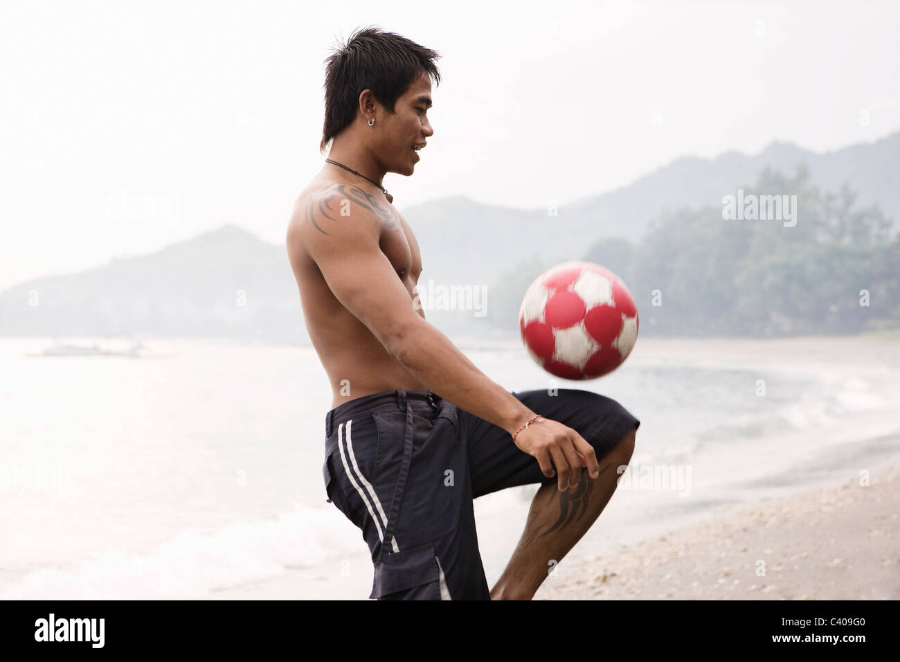 Guy playing football on beach Stock Photo - Alamy