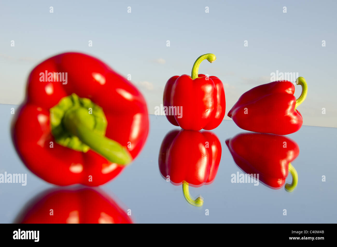 three red peppers on mirror and sky background Stock Photo - Alamy