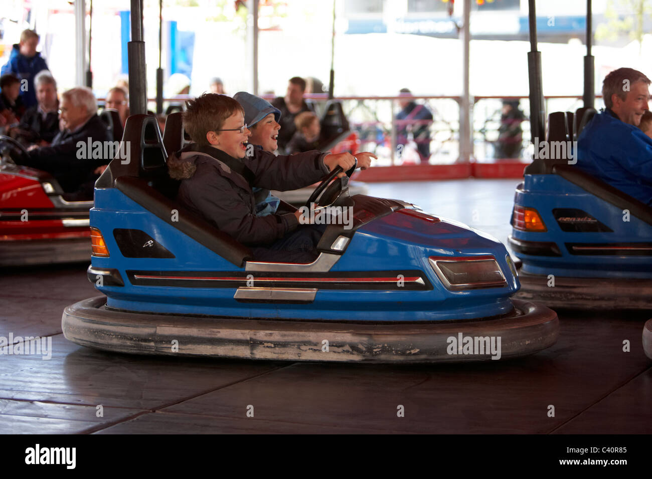 two young boys driving a dodgem bumper cars at a funfair in the uk ...