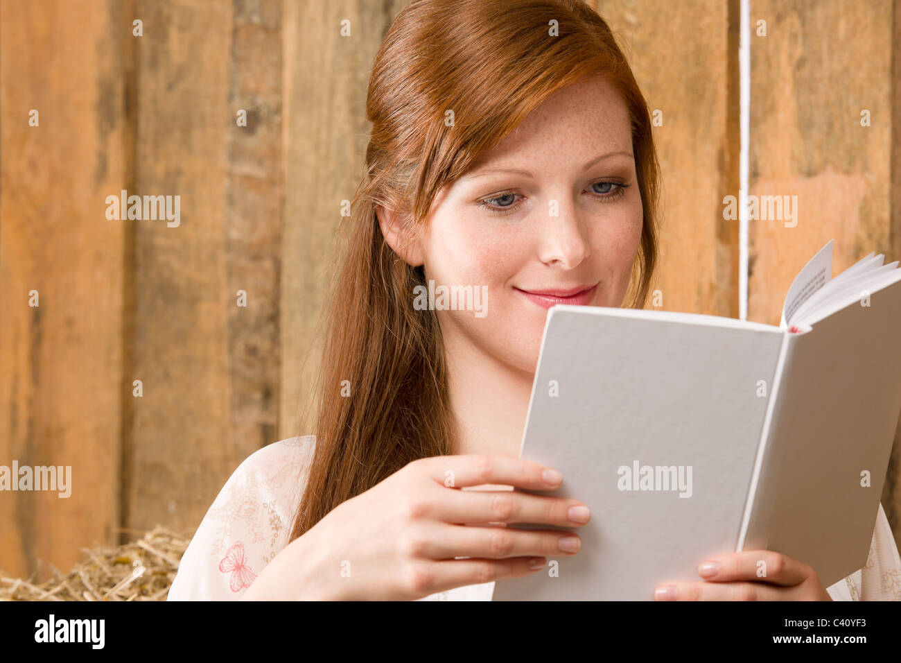 Young romantic red-hair woman reading book sitting in barn country ...