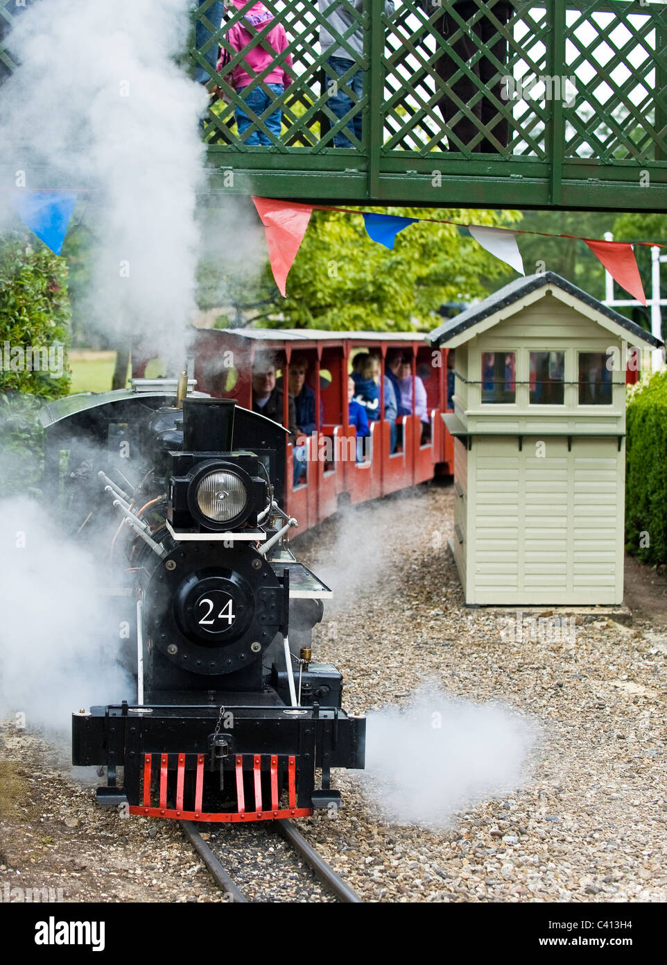 A miniature railway steam engine pulling carriages with passengers ...