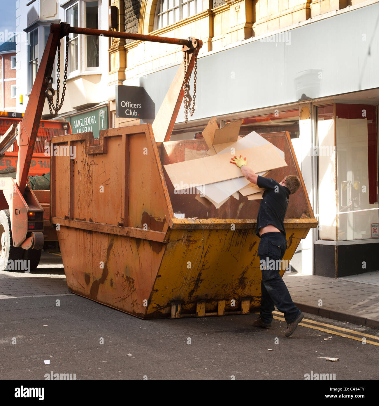 A Workman filling a high sided skip with waste from a shop ...