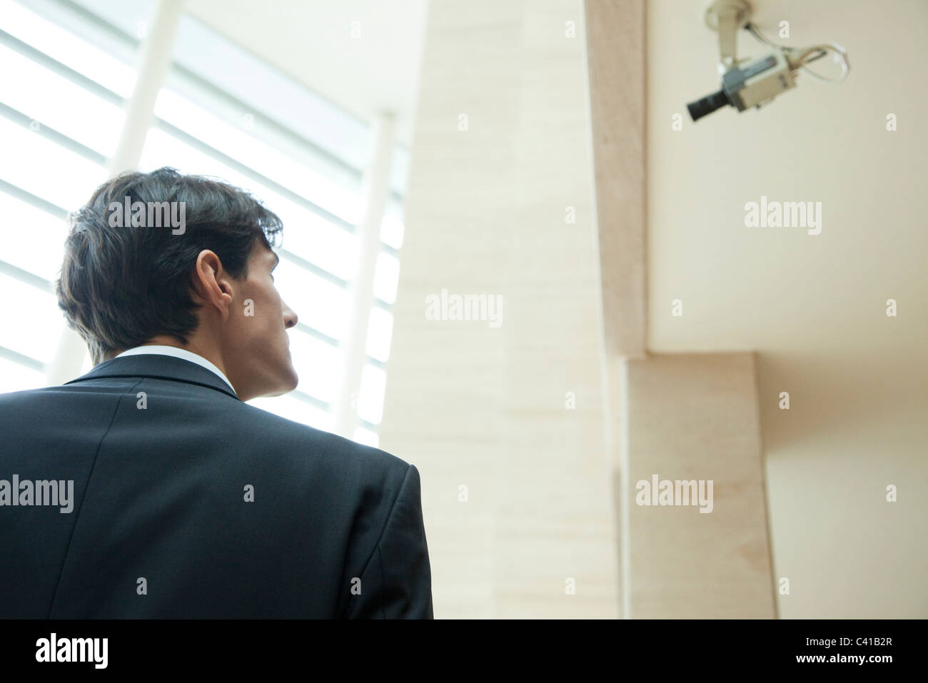 Businessman looking up at security camera Stock Photo - Alamy