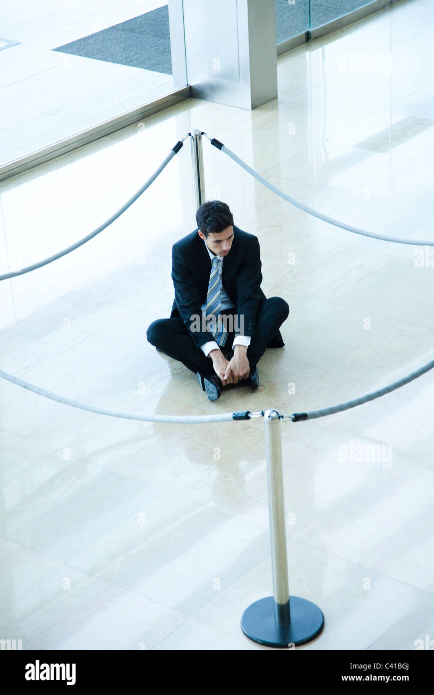 Businessman sitting on floor inside roped off area in lobby Stock Photo ...