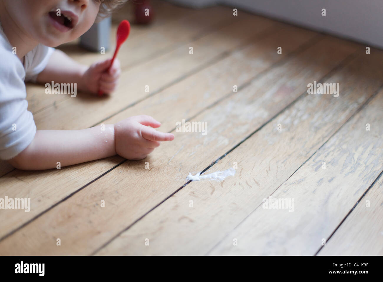 Toddler lying on floor with spoon in hand, pointing to spilled food ...