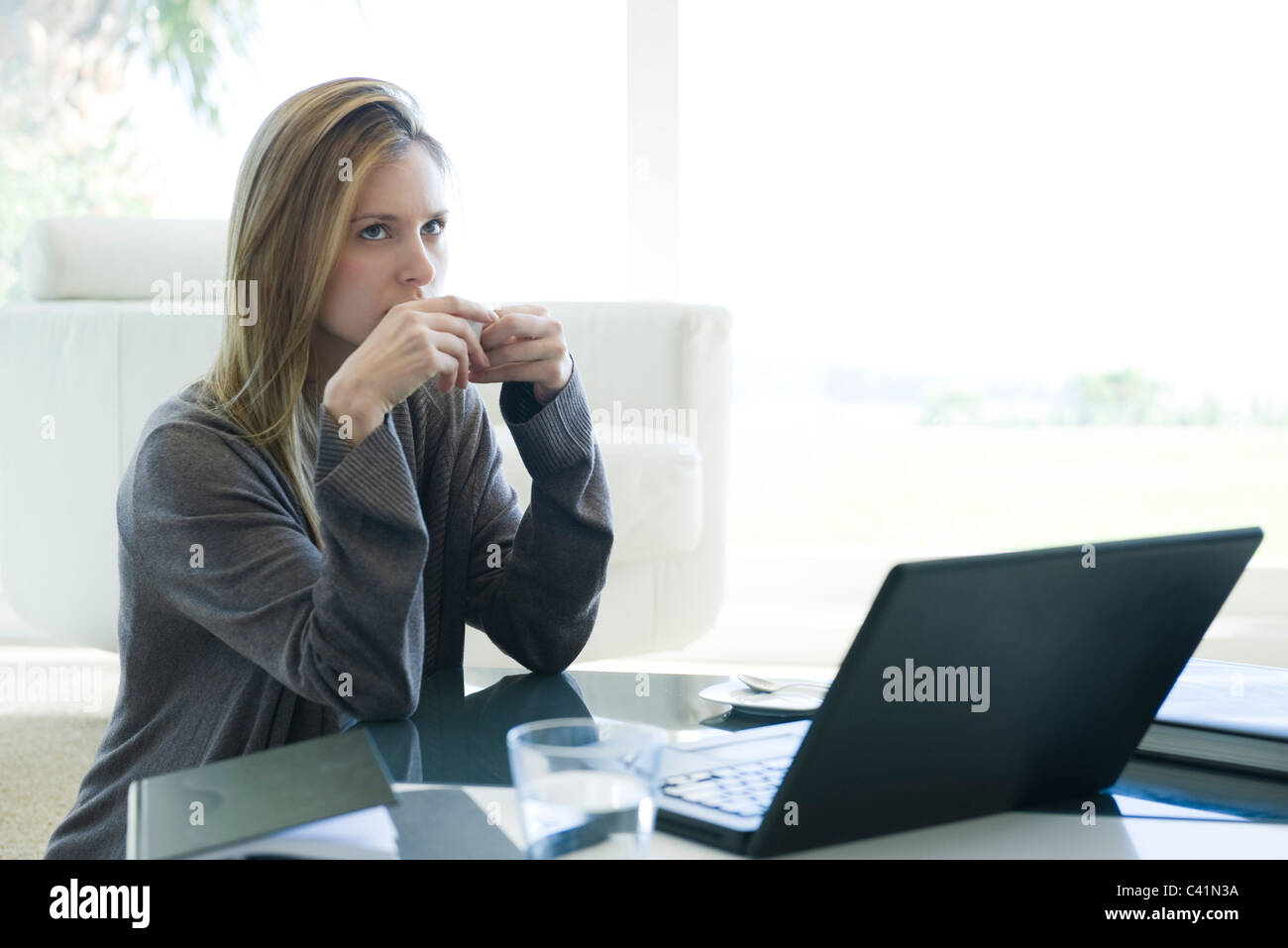 Woman sitting at coffee table with laptop computer, drinking coffee ...