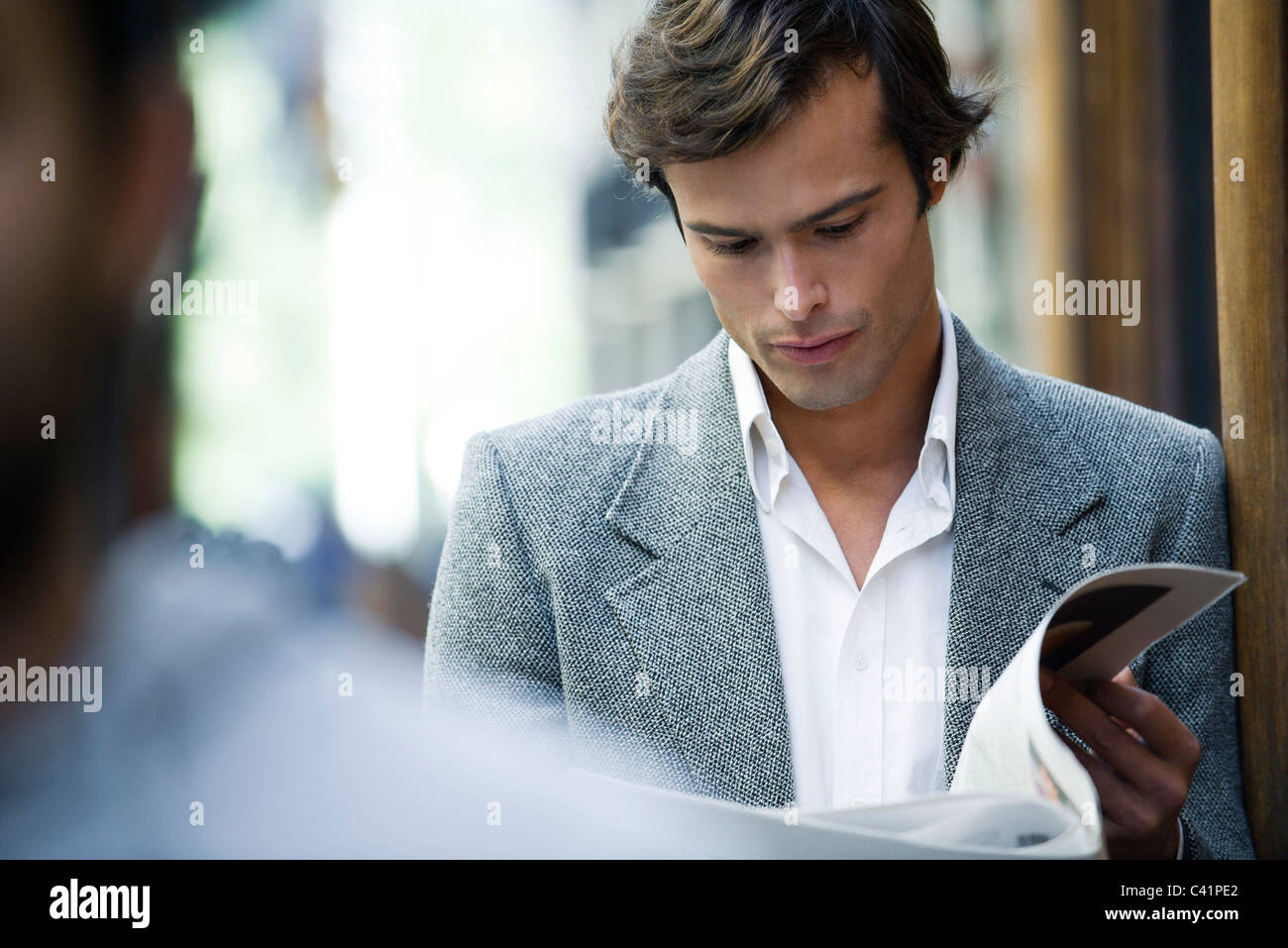 Man leaning against wall reading newspaper Stock Photo - Alamy