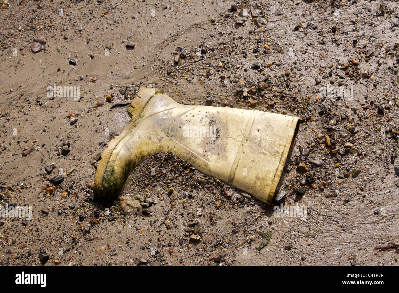 A lone yellow wellington (welly) boot discarded in the sand and mud at ...