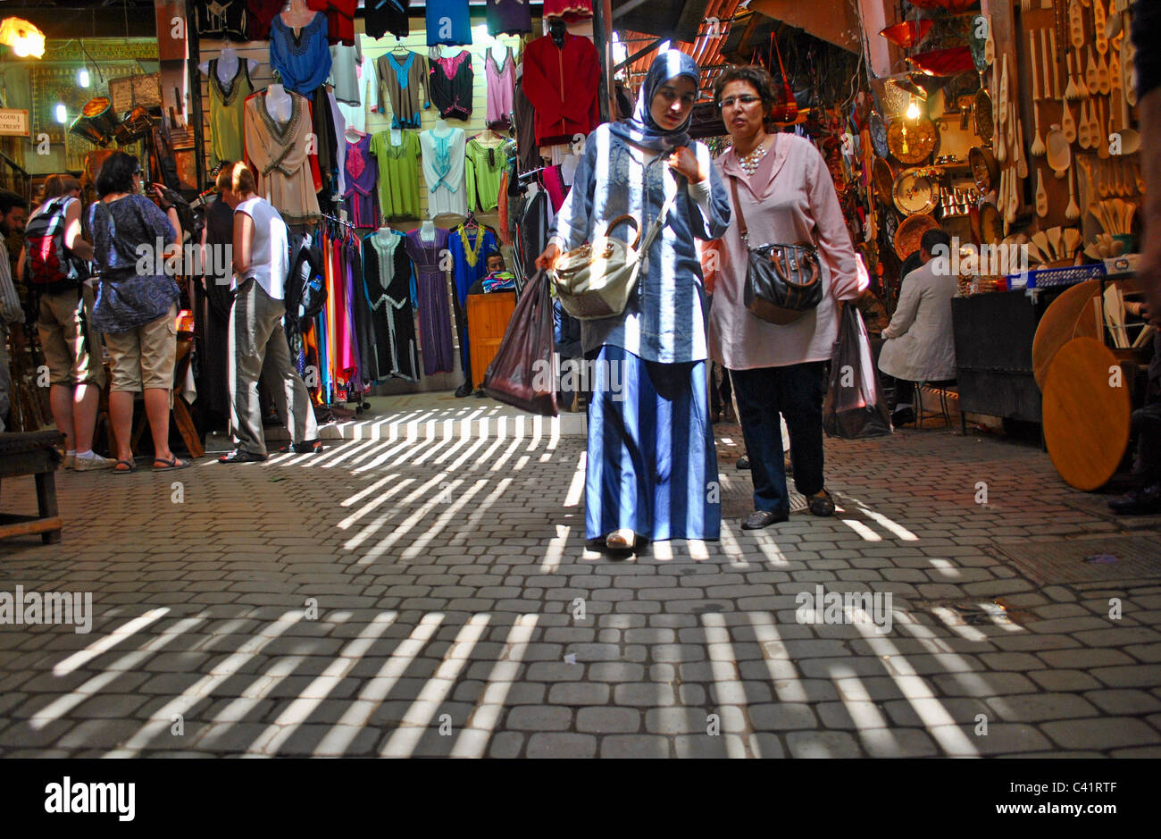 Women walk through a souk in Marrakesh as light streams through slats ...