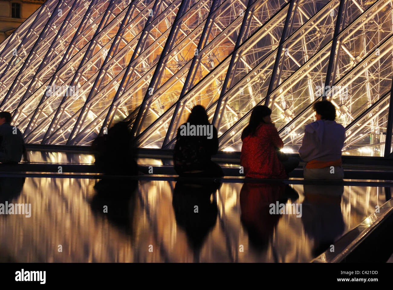 Four people sitting by the famous glass pyramid in the Louvre Museum ...