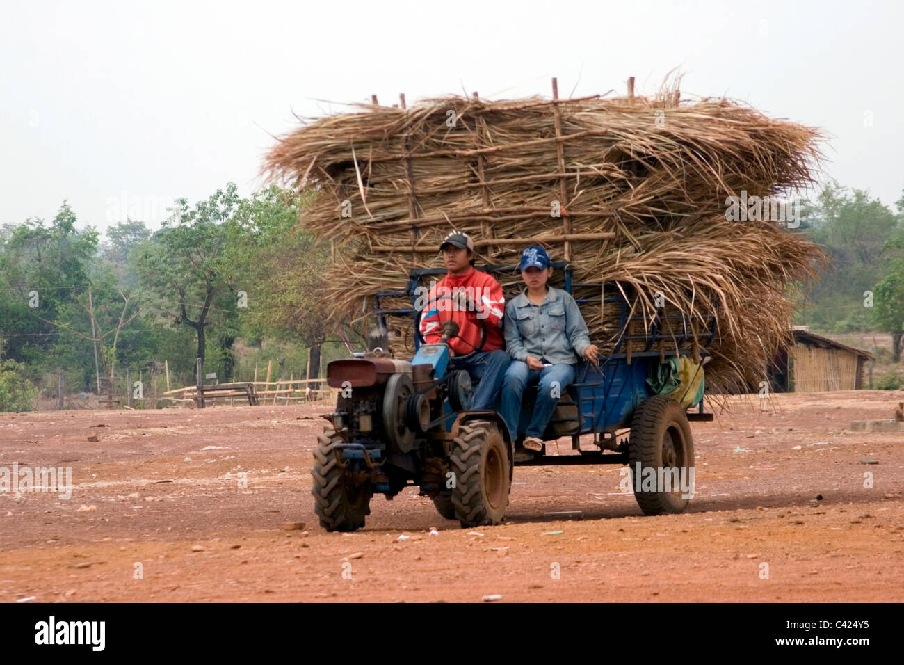 A man and a woman riding a tractor are transporting a large load of ...