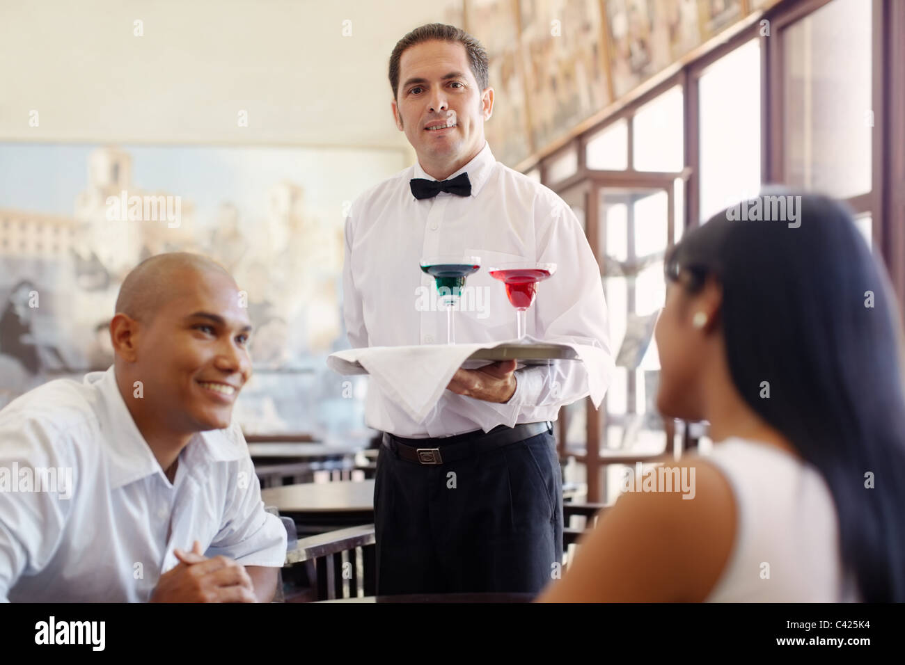 hispanic waiter serving adult couple at table in restaurant and looking ...