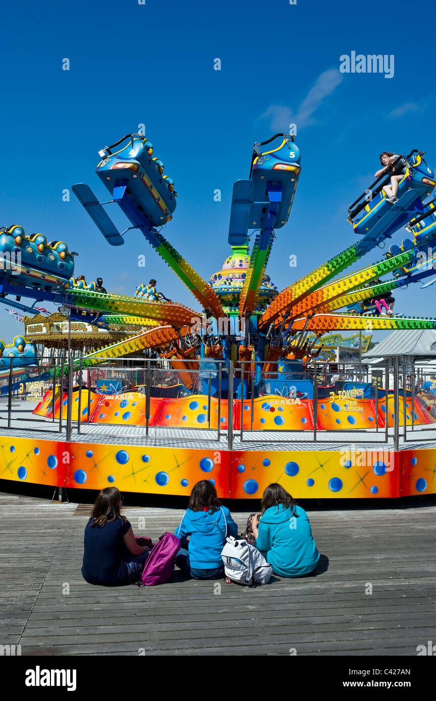 Three young girls sitting in front of a fairground ride on Brighton ...