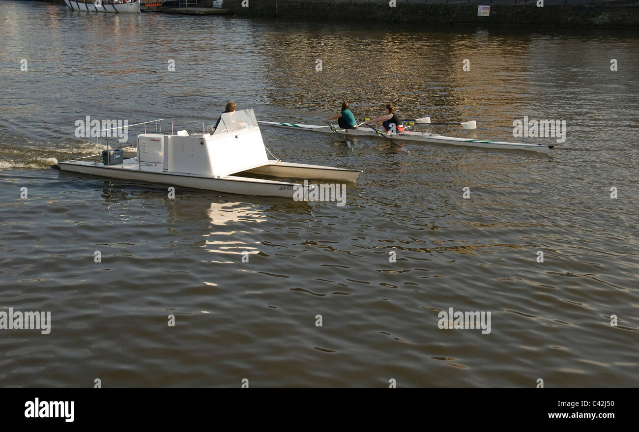 Two women in rowing boat accompanied by coach in motor boat, harbour ...