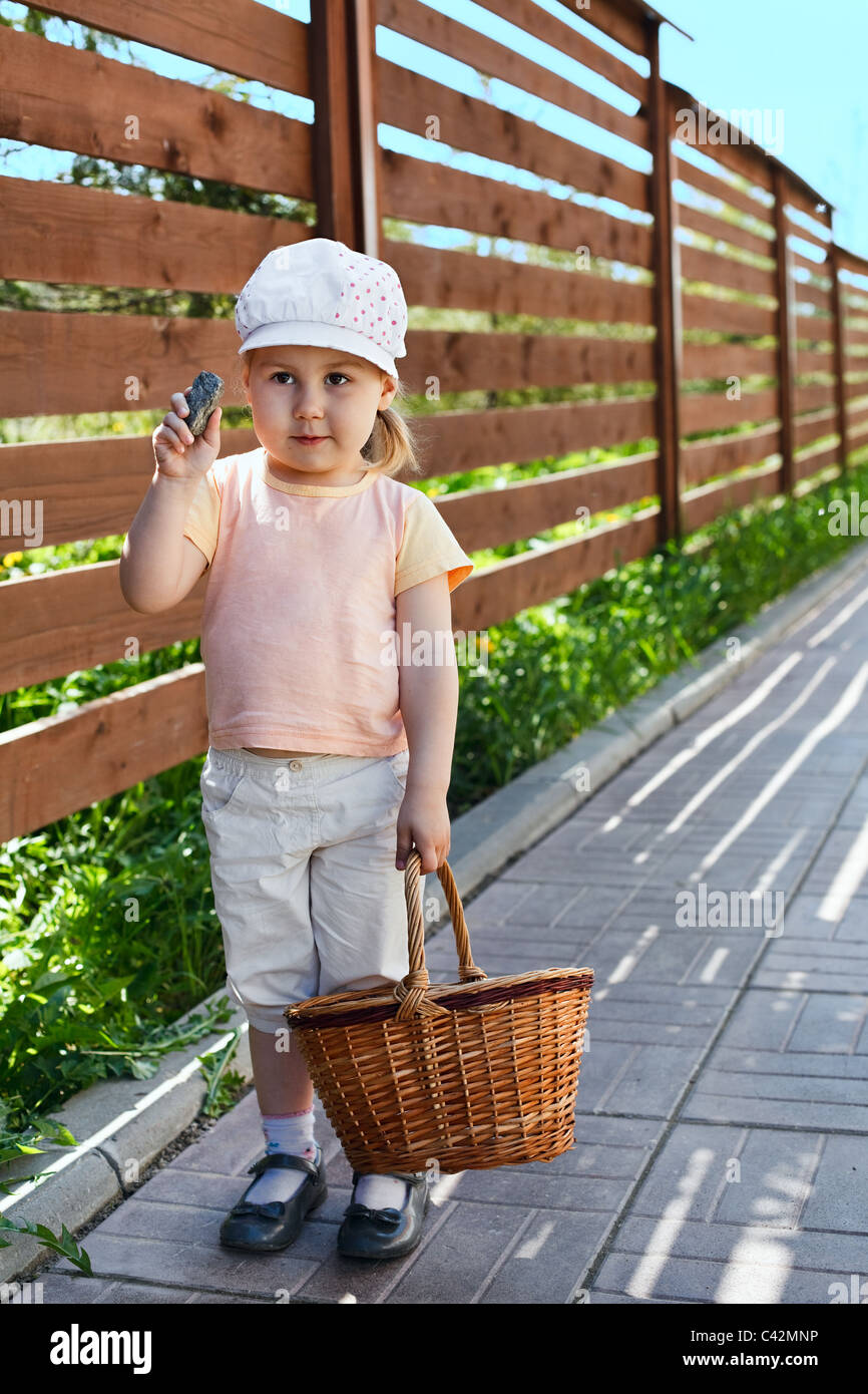 Little Russian child standing with basket in summer time near a fence ...