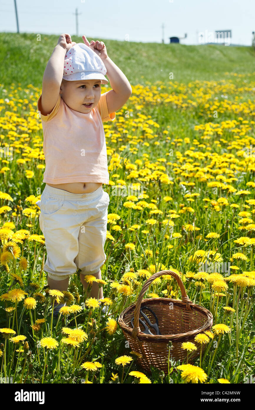 Little Russian child standing on field of yellow flowers with basket ...