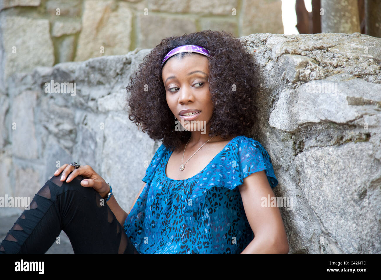 Pretty black woman outside leaning against a stone wall Stock Photo - Alamy