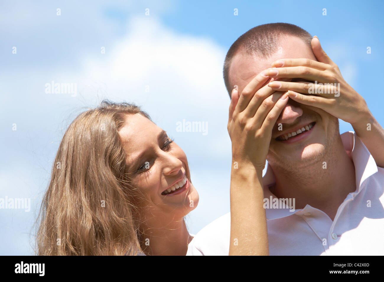 Laughing female keeping her hands on male’s eyes and looking at him ...