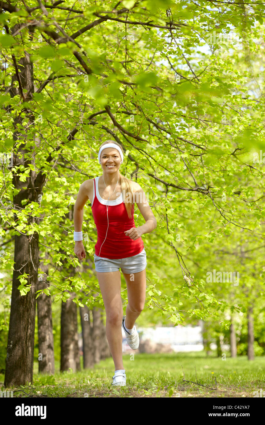 A young girl jogging in the park along green trees Stock Photo - Alamy