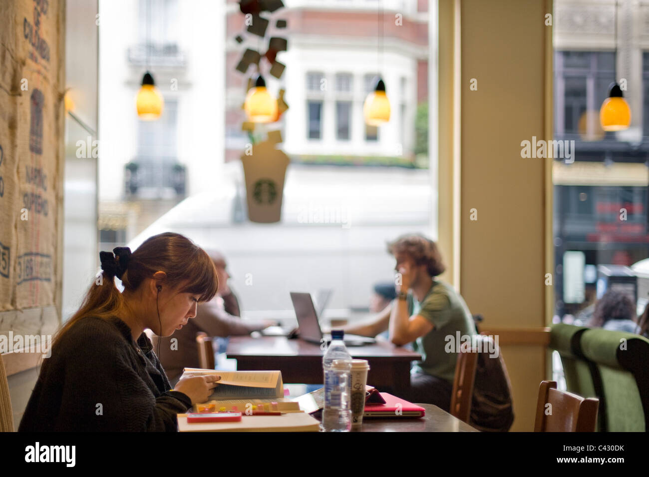 A young woman sits studying in Starbucks with a coffee whilst listening ...