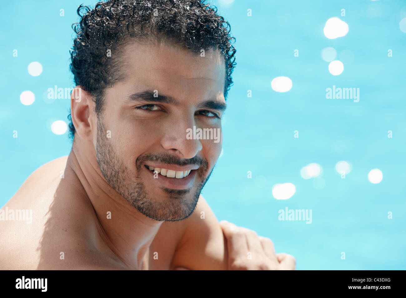 Handsome happy young hispanic man smiling and relaxing near hotel pool ...