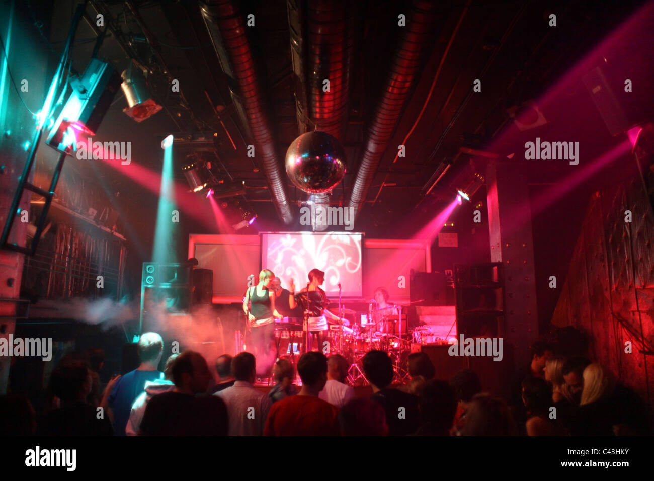 A crowd of people watching live music performance lit with spotlights ...