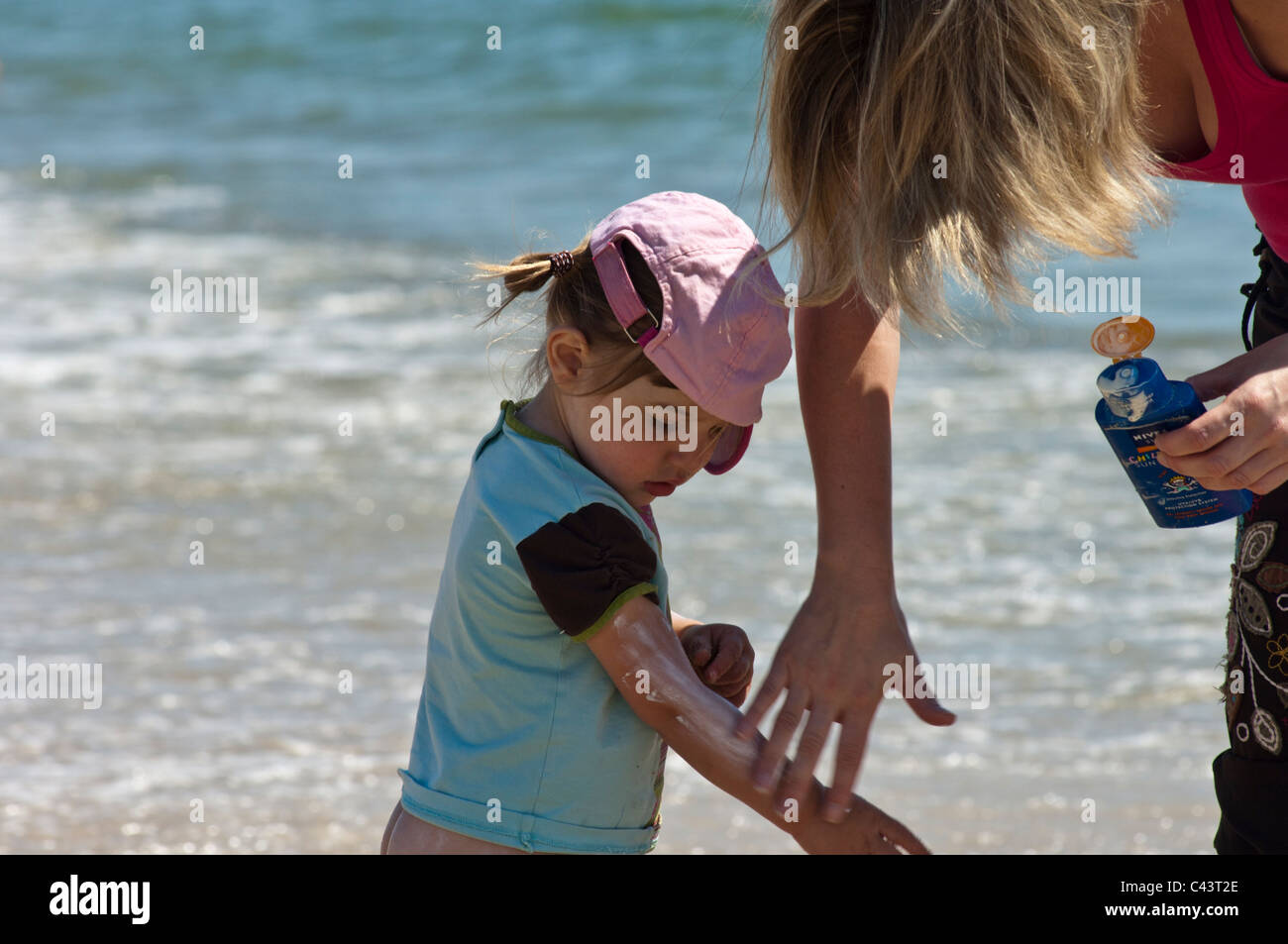 applying sun cream near the shoreline on the beach on a childs arm ...