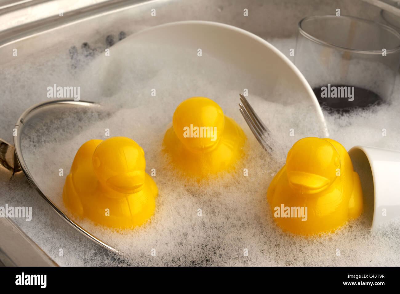three yellow plastic toy ducks floating in a sink full of washing up ...