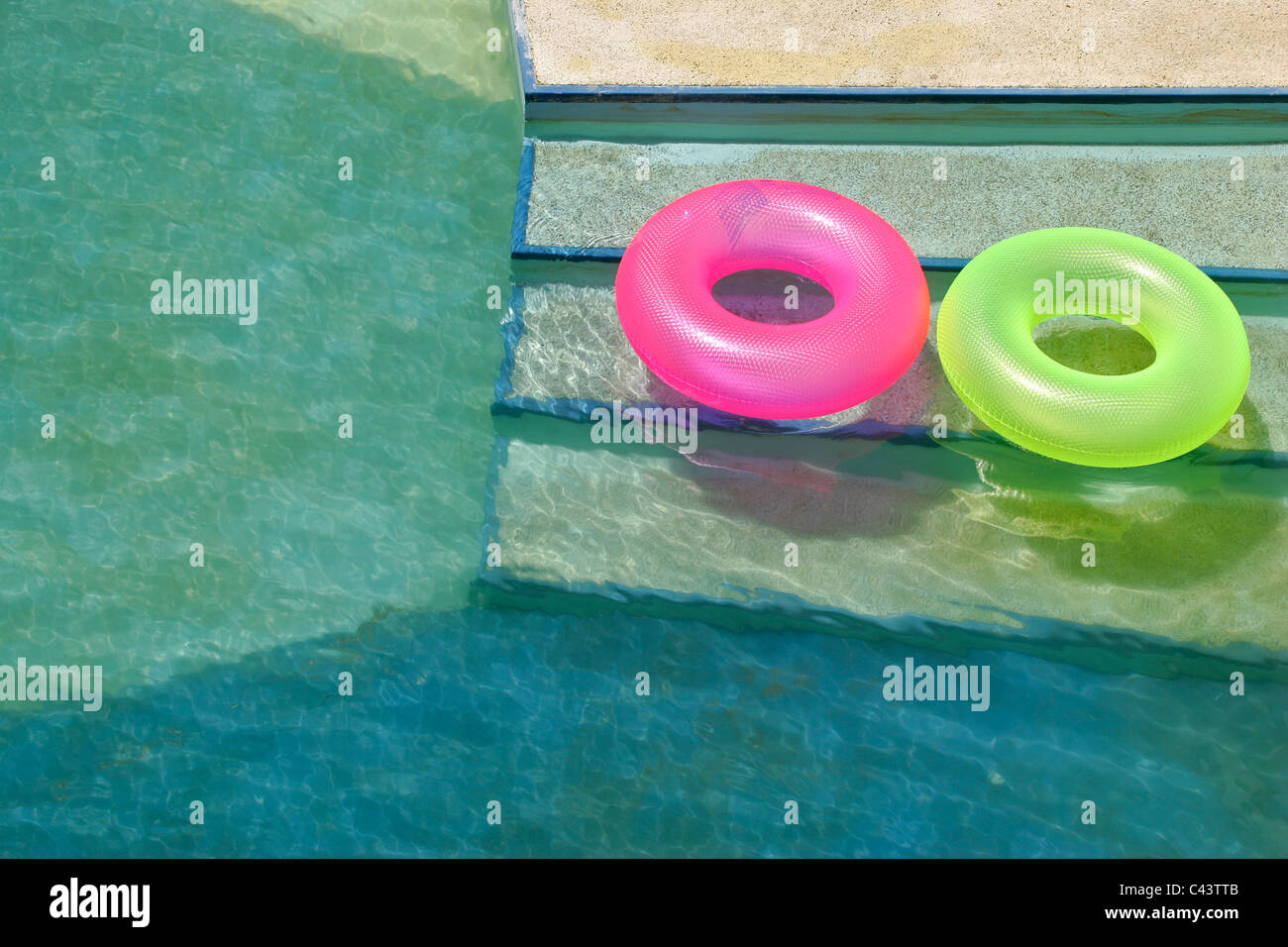 Two colorful pink and green ring lilo floaters in outdoor swimming pool ...