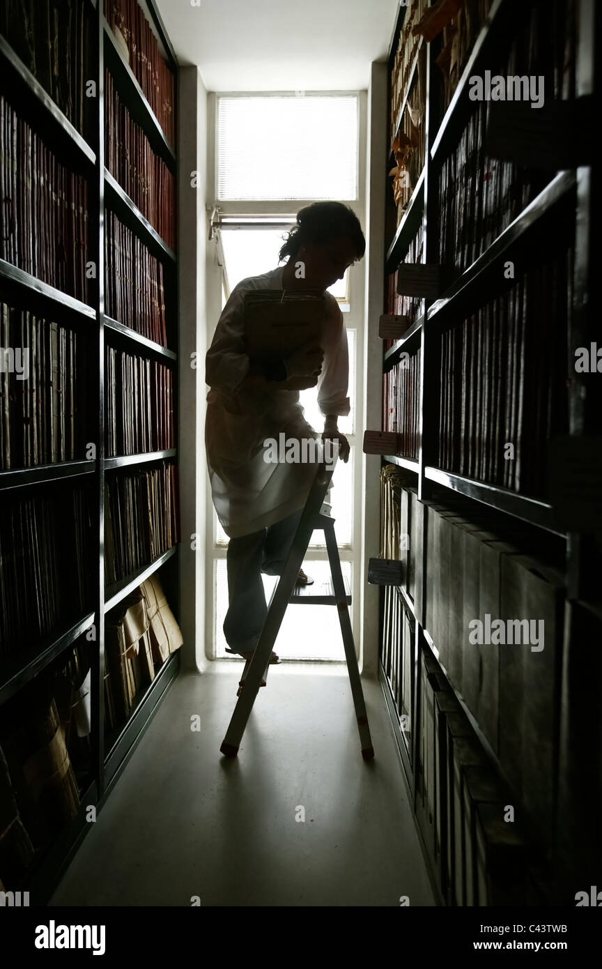 Silhouette of person on top of stepladder retrieving books from library ...