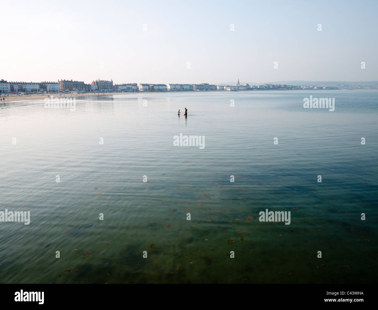 two lone bathers in the sea off Weymouth, Dorset England with the coast ...