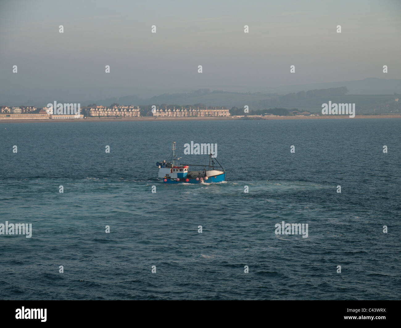 fishing boat makes its way out to sea at dawn off Weymouth Doreset ...