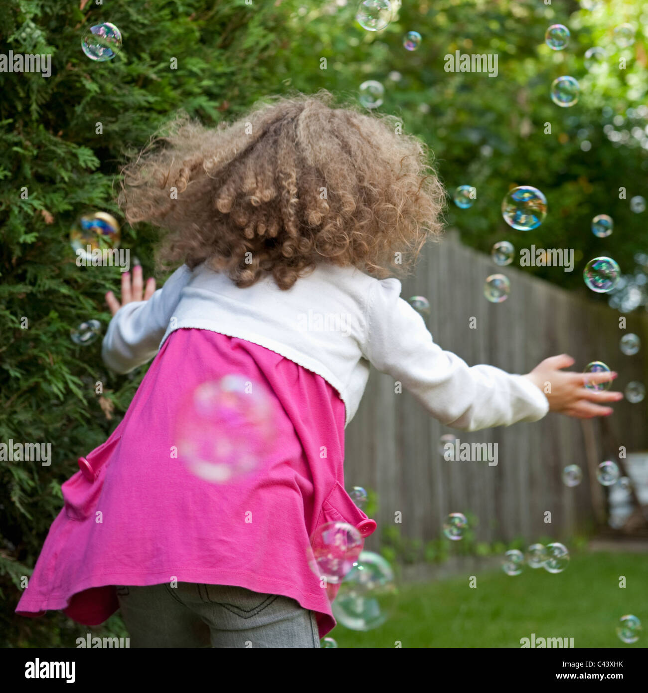 A little girl plays in her garden trying to catch bubbles Stock Photo ...