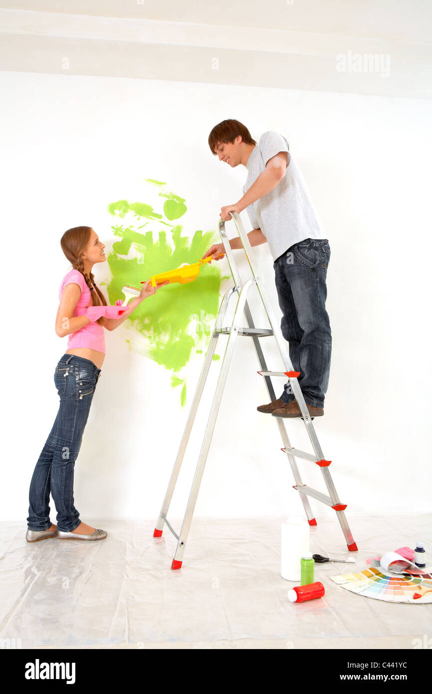 Young guy and girl helping each other to paint walls in new house Stock ...