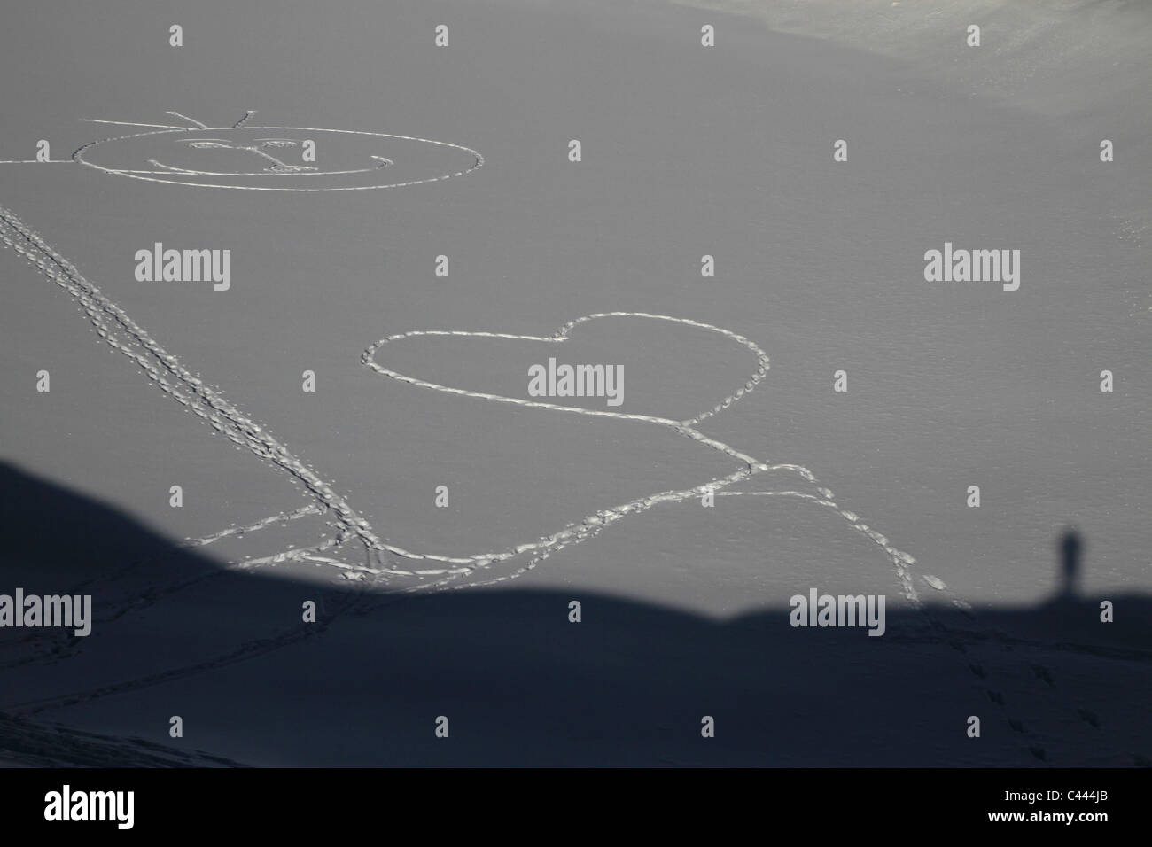 A heart shape and smiley face stamped out in the snow by footprints ...