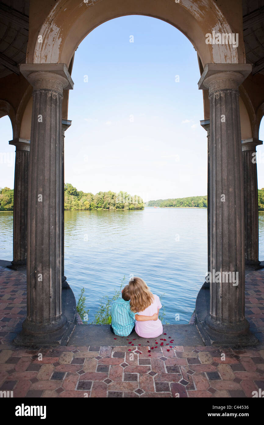 Two children sitting together under an arch next to a lake Stock Photo ...