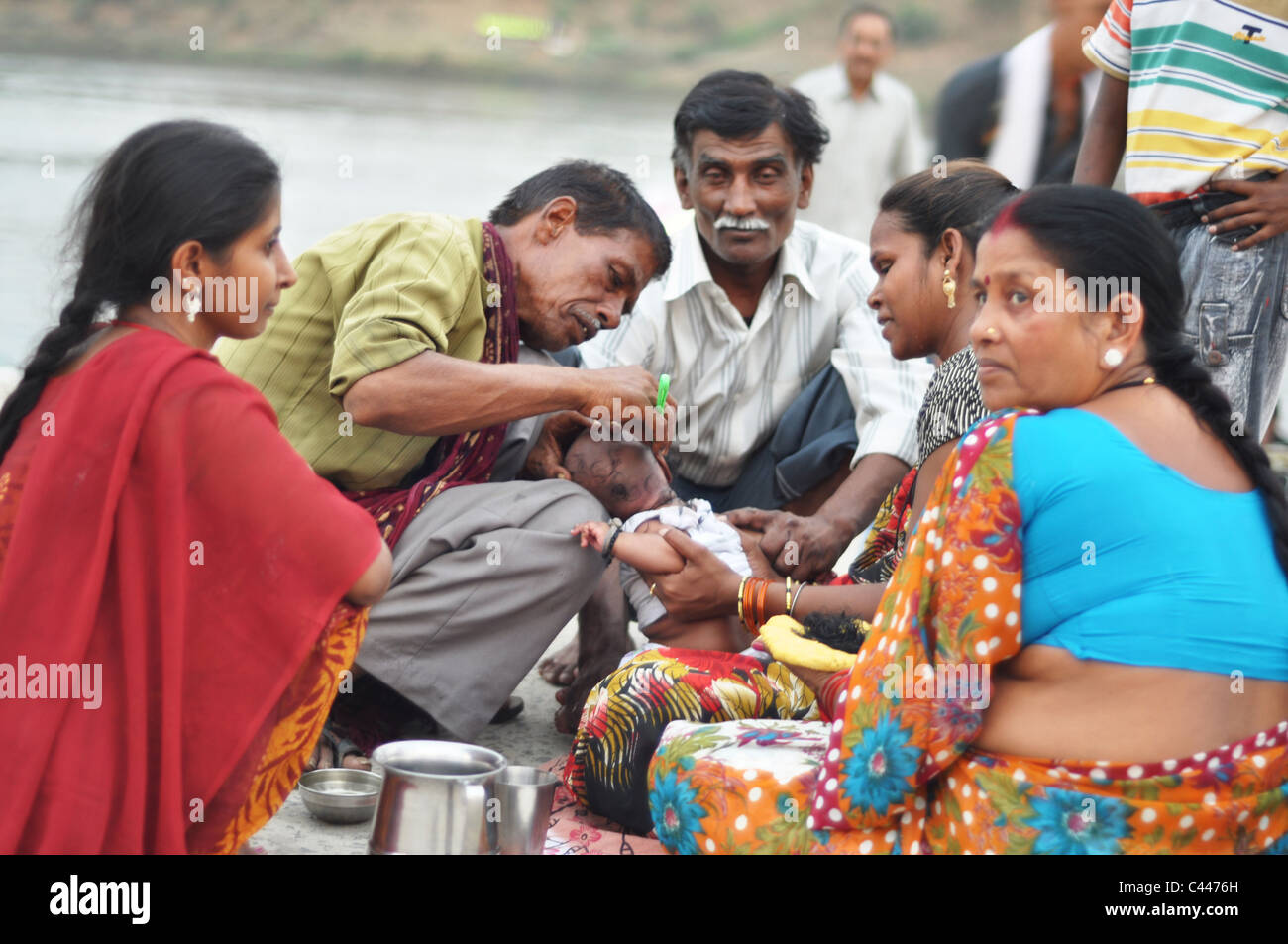 A Barber shaving head of a baby on the banks of River Narmada in ...