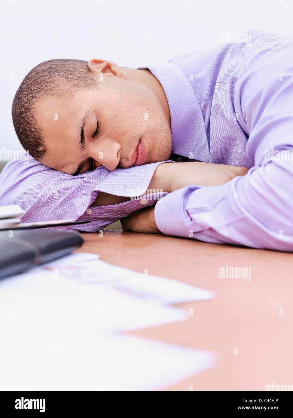 A businessman with his head resting on his arm, eyes closed, outdoors ...